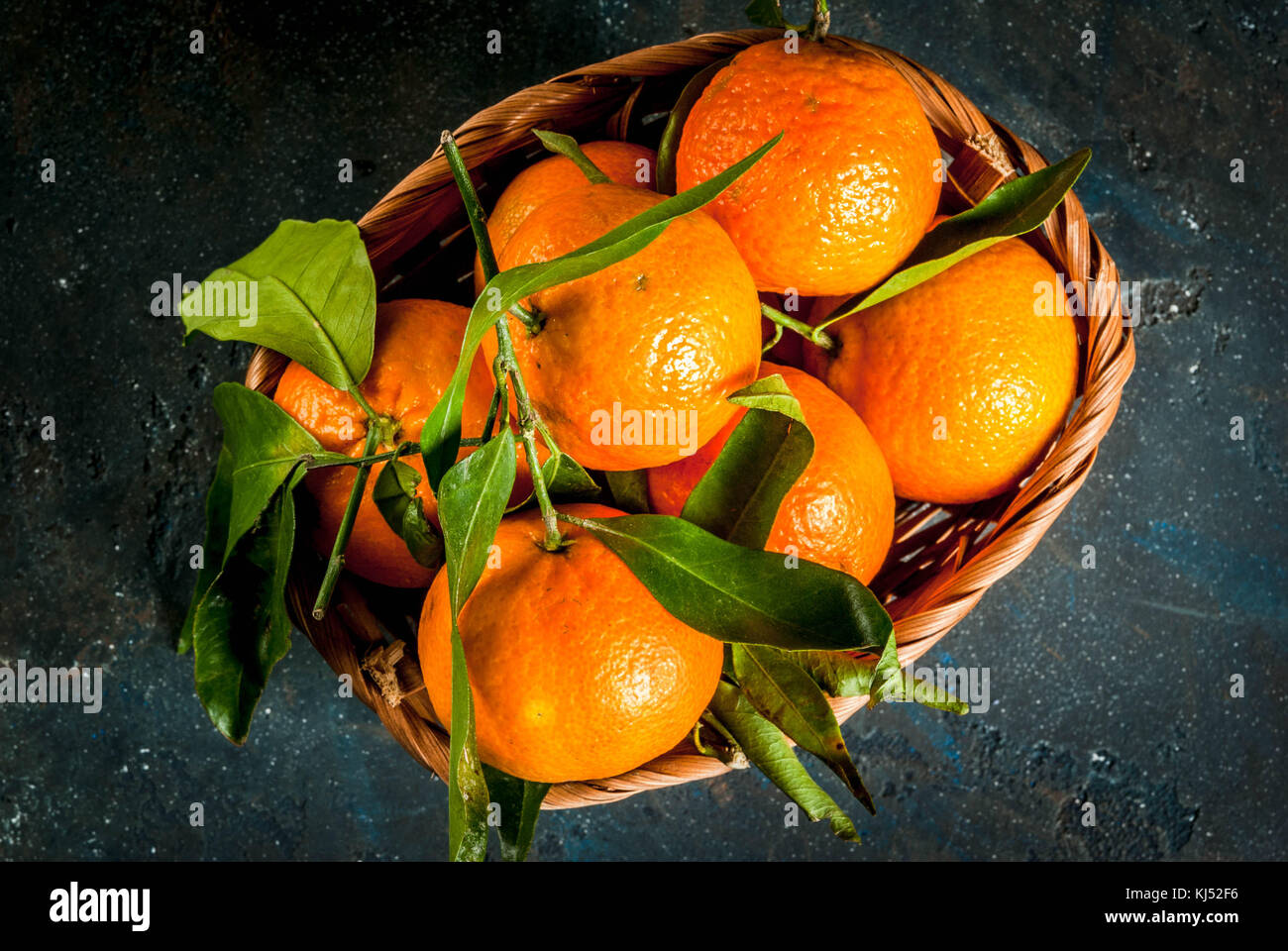 Fresh raw organic Tangerines with green leaves in little basket on dark ...