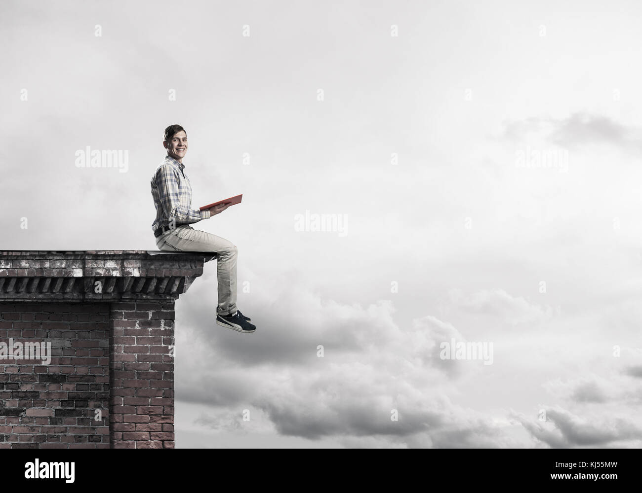 Man on roof edge reading book and cloudscape at background Stock Photo ...