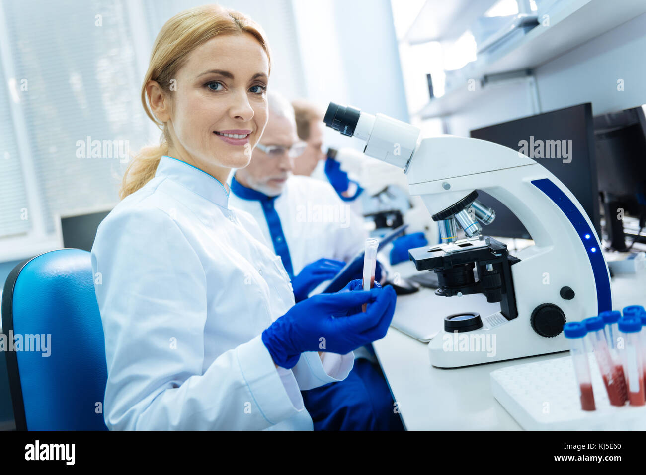 Smiling scientist sitting at a microscope Stock Photo - Alamy