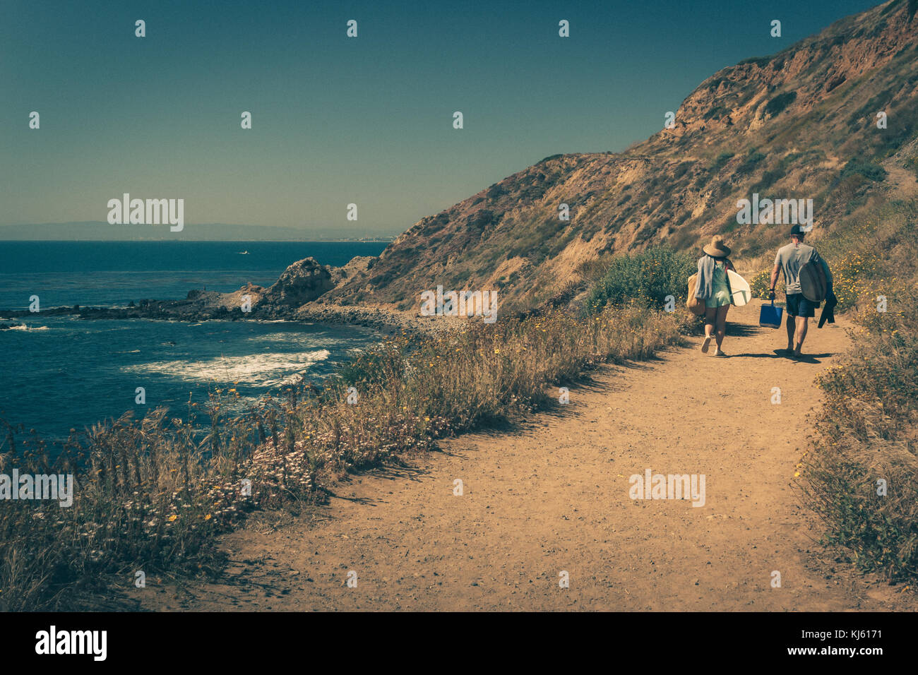 Young couple walking on a rugged trail with their surfboards in Palos ...