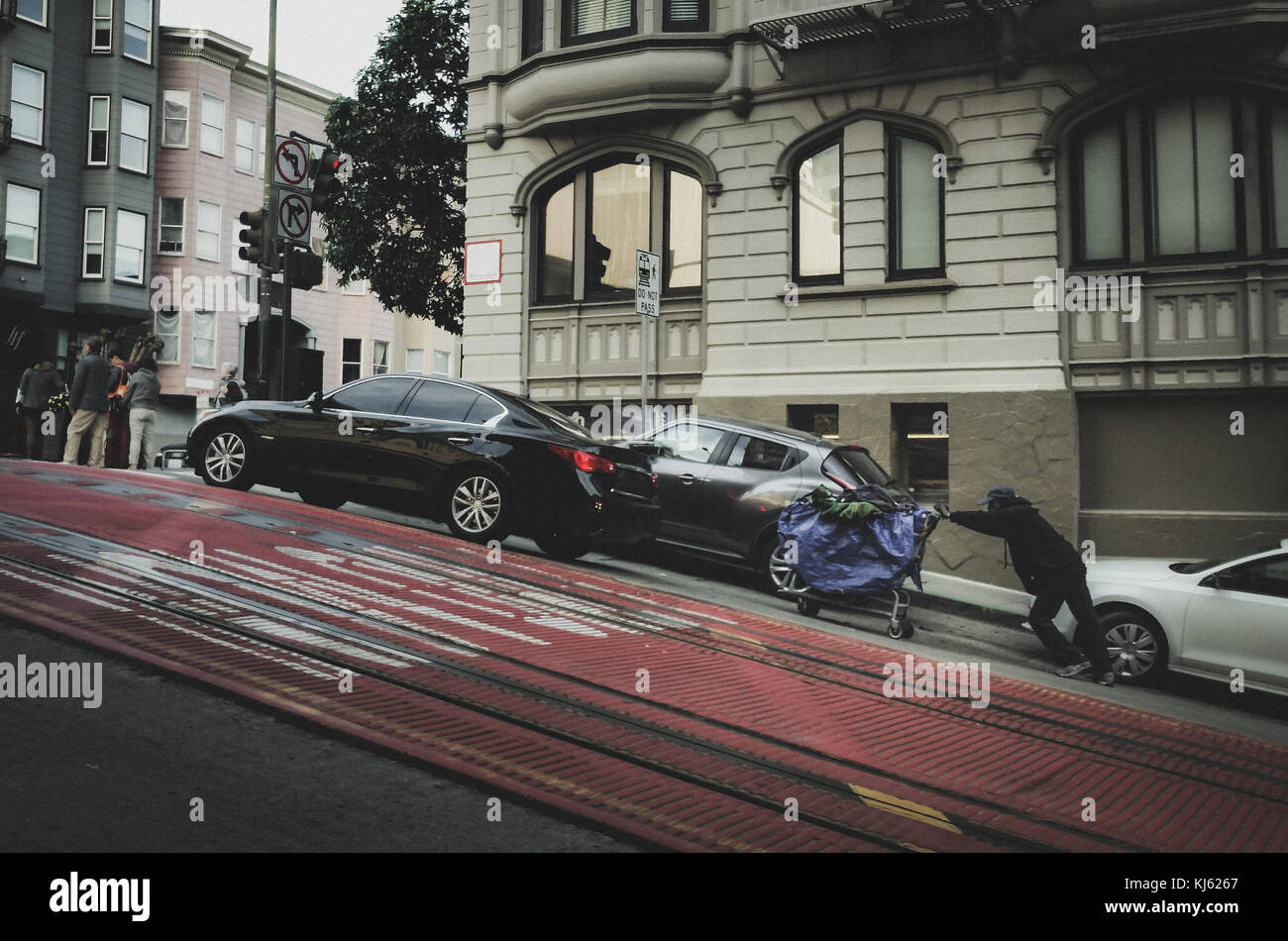 Homeless man pushing a shopping cart uphill on a steep hill in San ...