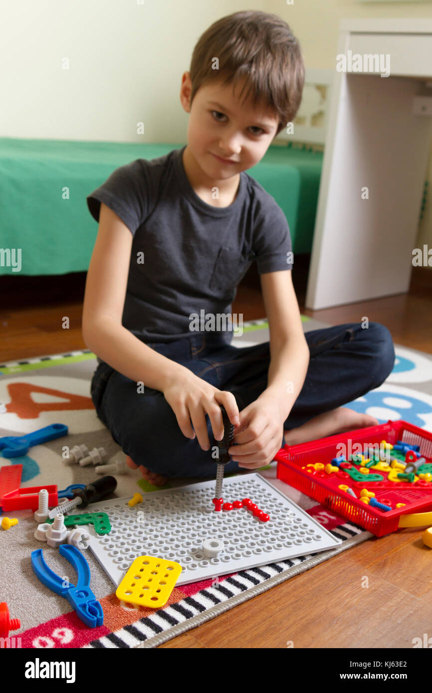 Smiling boy playing with toys tool kit while sitting on the floor in ...
