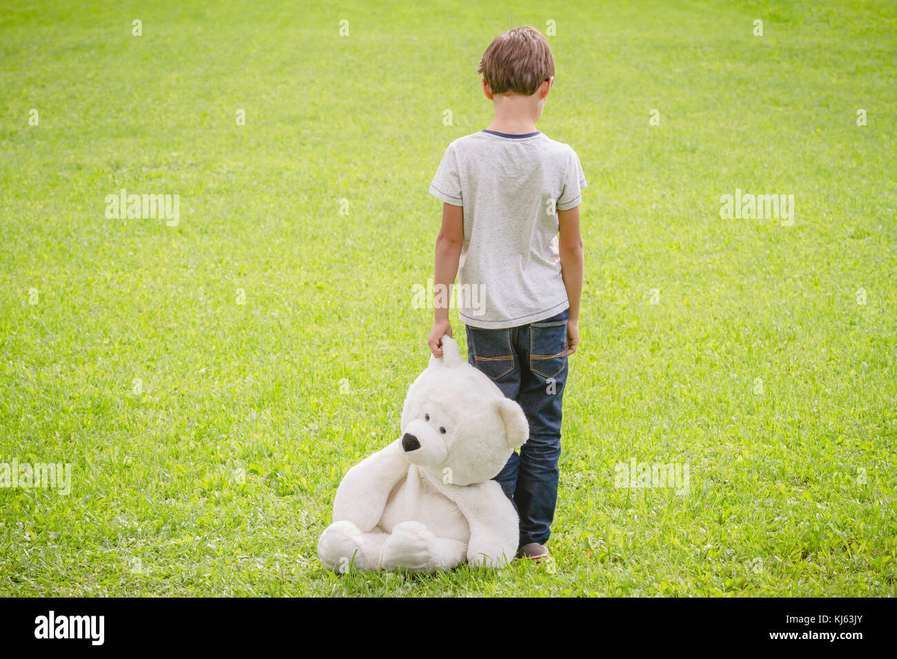 Sad child with teddy bear standing in the meadow. Child looking down ...