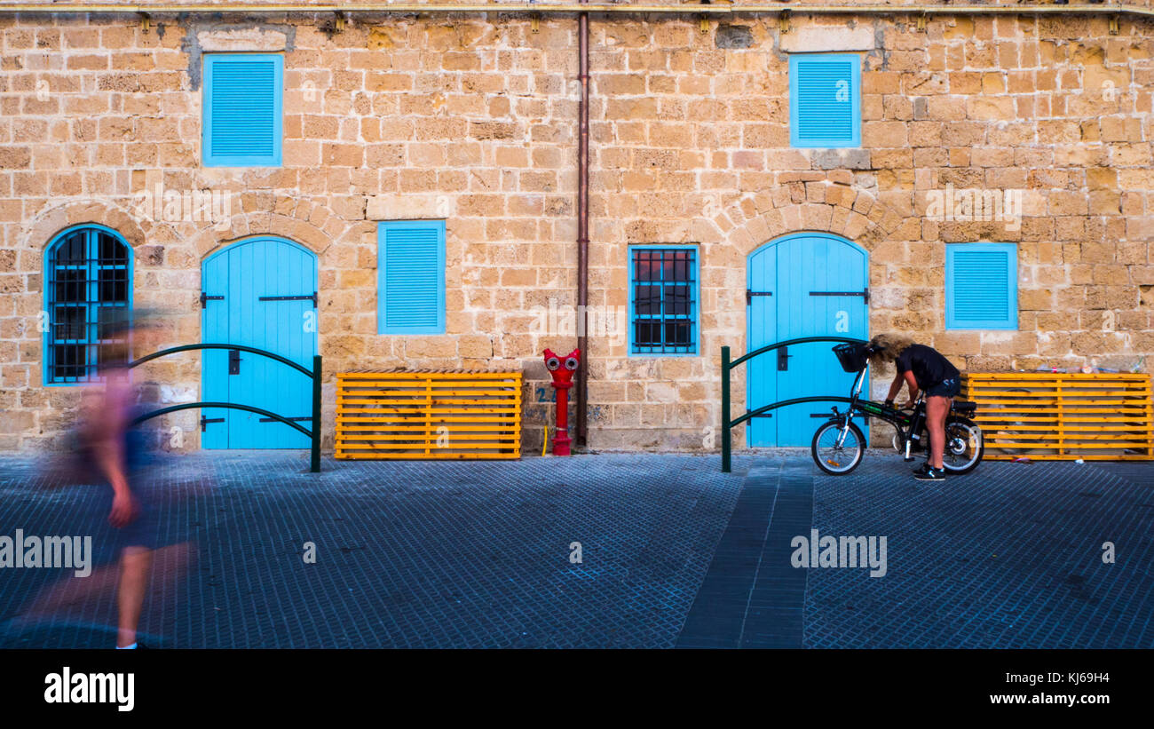 walking woman and static women with bicycle at the front of old stone ...