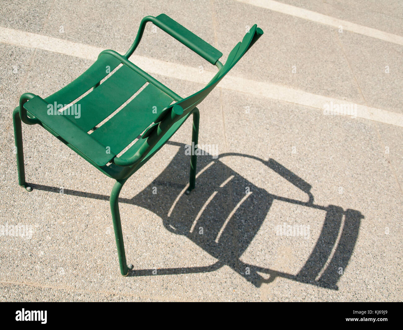 Green chair casting shadow on the pavment Stock Photo - Alamy