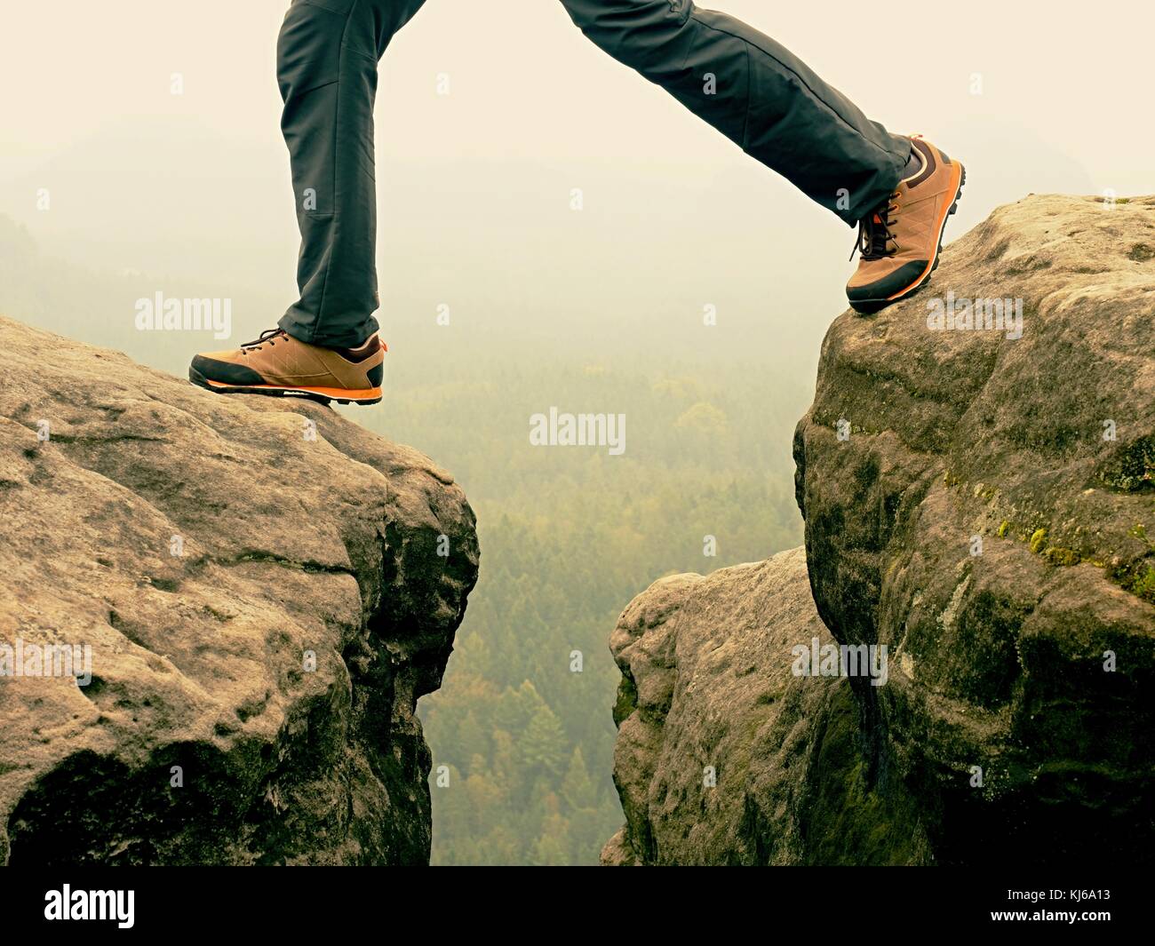 Male legs in dark hiking trousers and leather trekking shoes on peak of ...