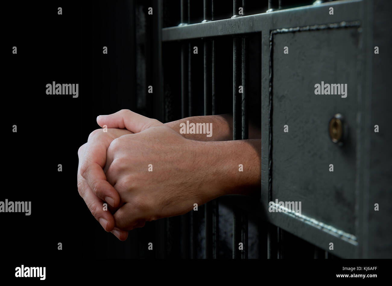 A closeup of a dimly lit prison holding cell door with arms reaching ...