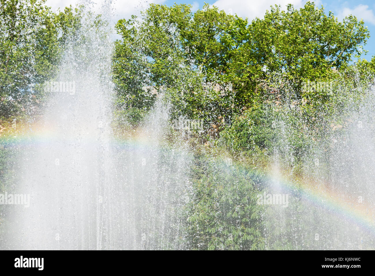 rainbow over water in fountain with green trees on background ...