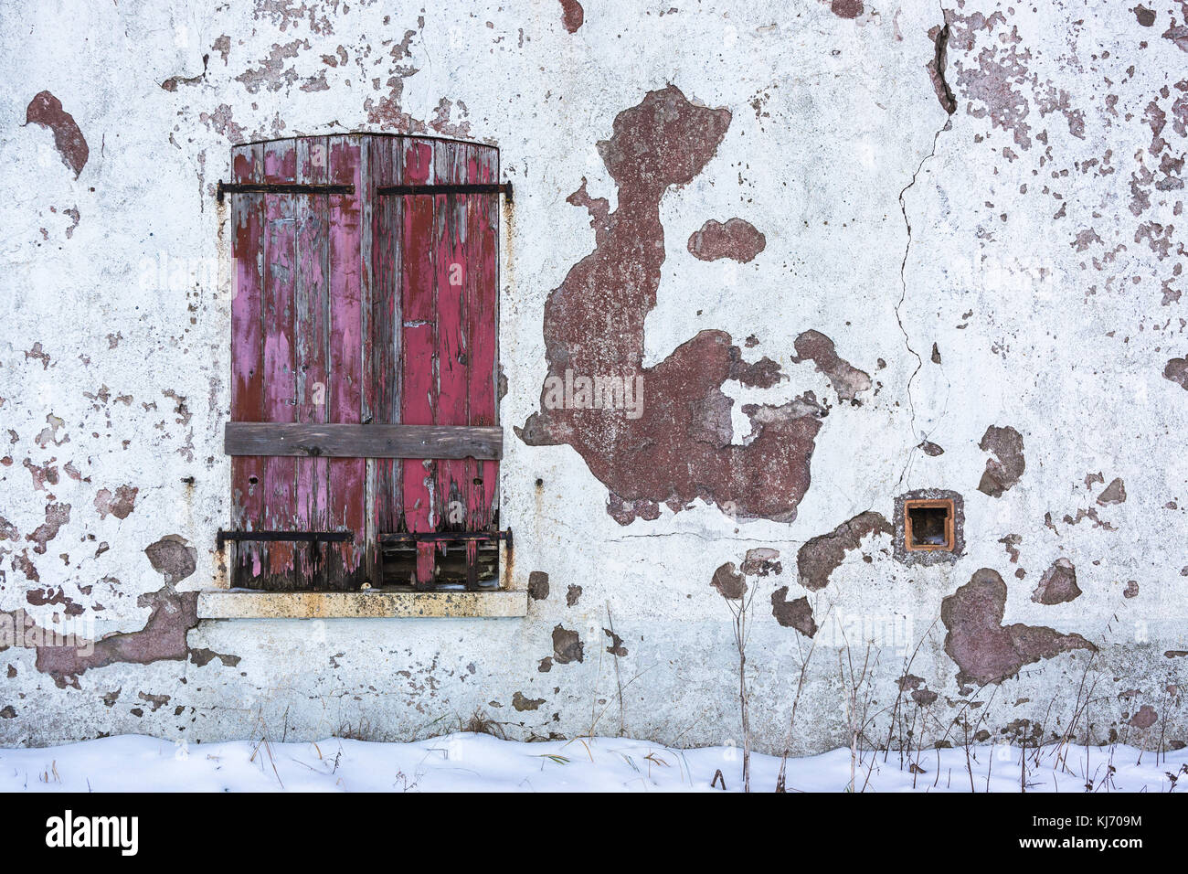 An old window with closed red worn wooden shutters on a white decrepit ...