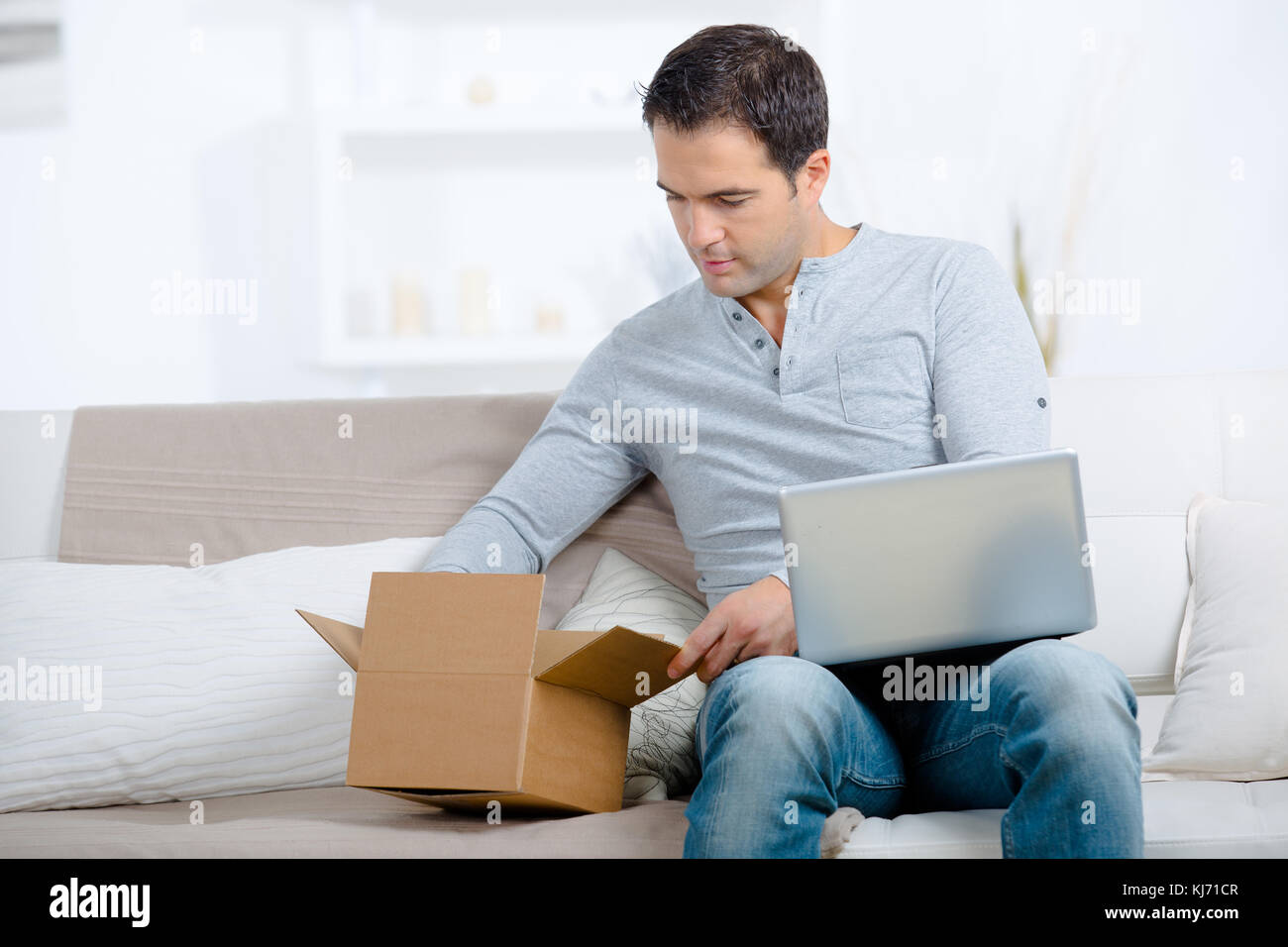 young man with laptop computer opening parcel box Stock Photo - Alamy