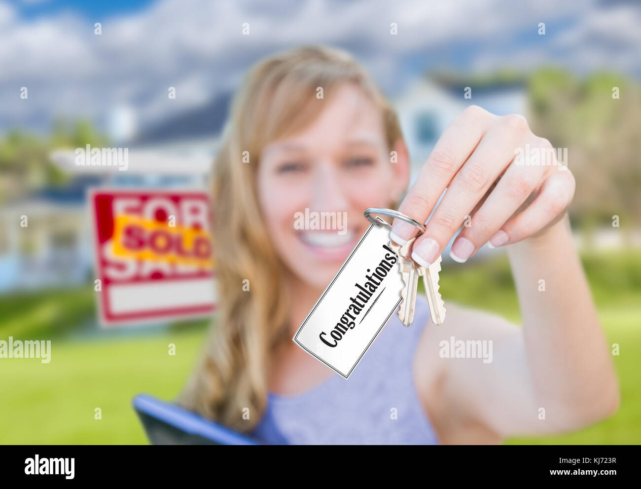 Woman Holding New House Keys with Congratulations Card In Front of Sold ...