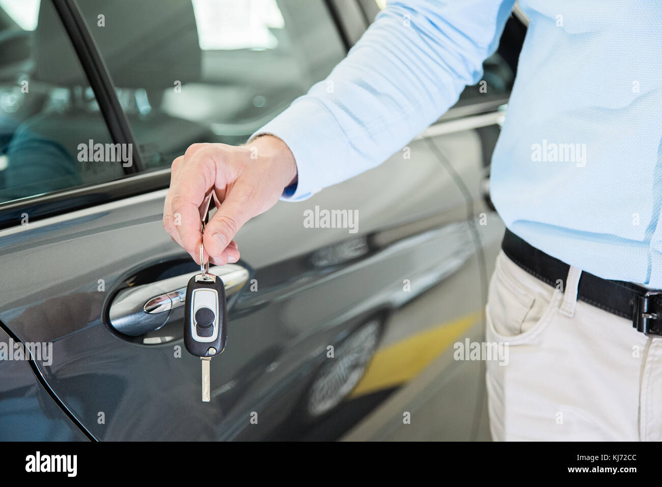 Close up photo of male car dealer hand holding a car key next to a car ...