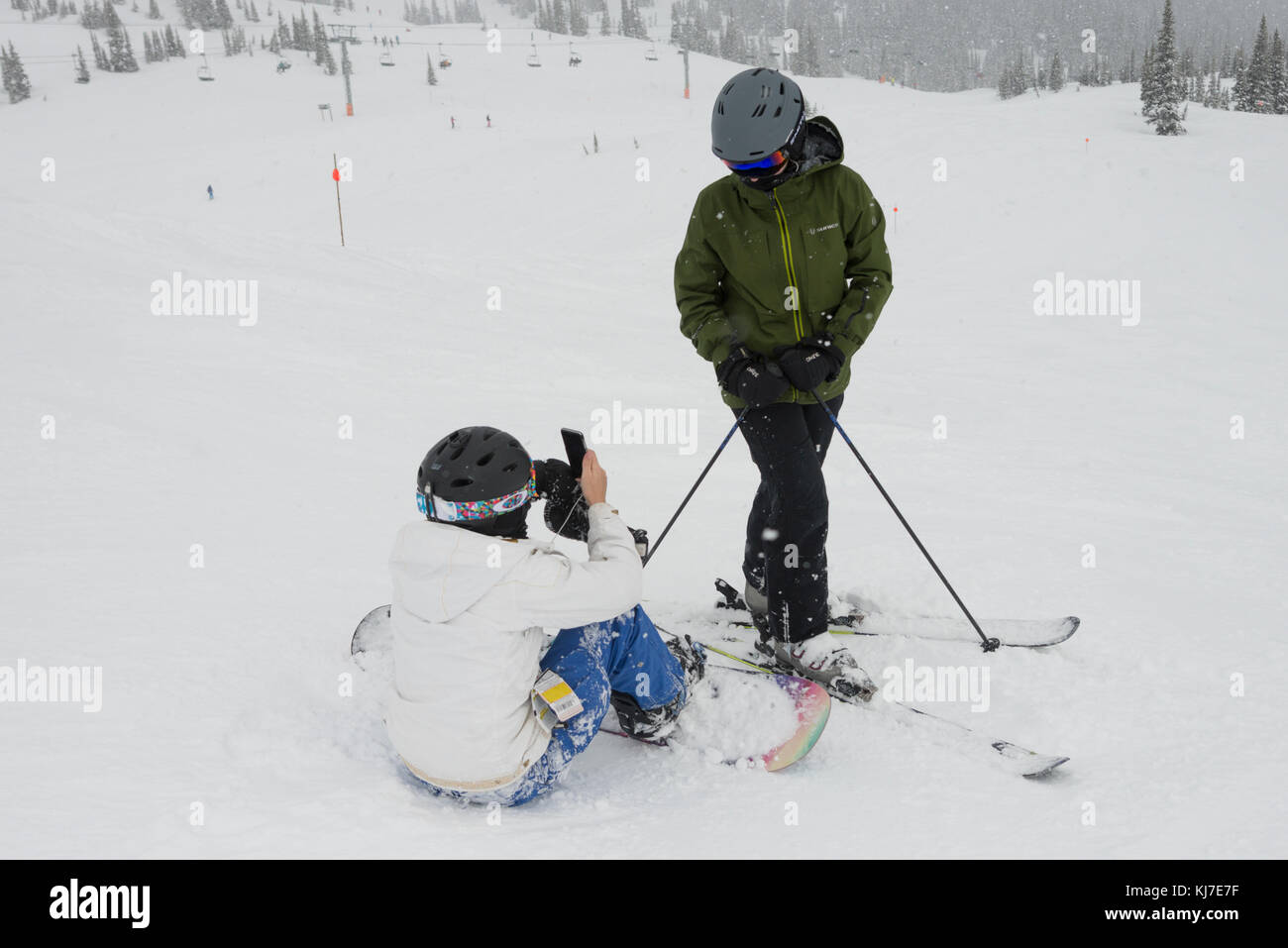 Snowboarder using smart phone on snowy mountain with skier,Whistler ...