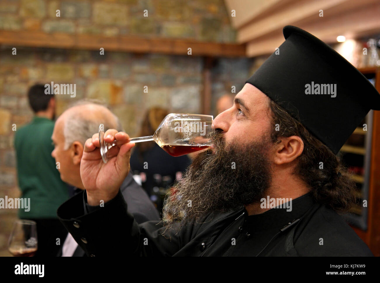 Greek Othodox priest tasting some red wine in the winery of Toplou ...