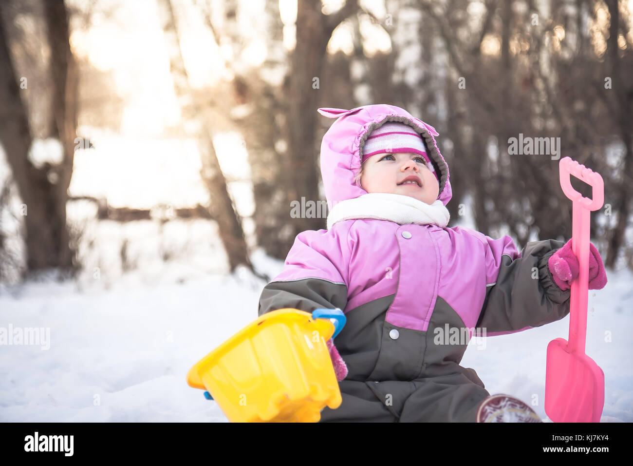Cheerful child playing with snow in cold sunny winter day in warm ...