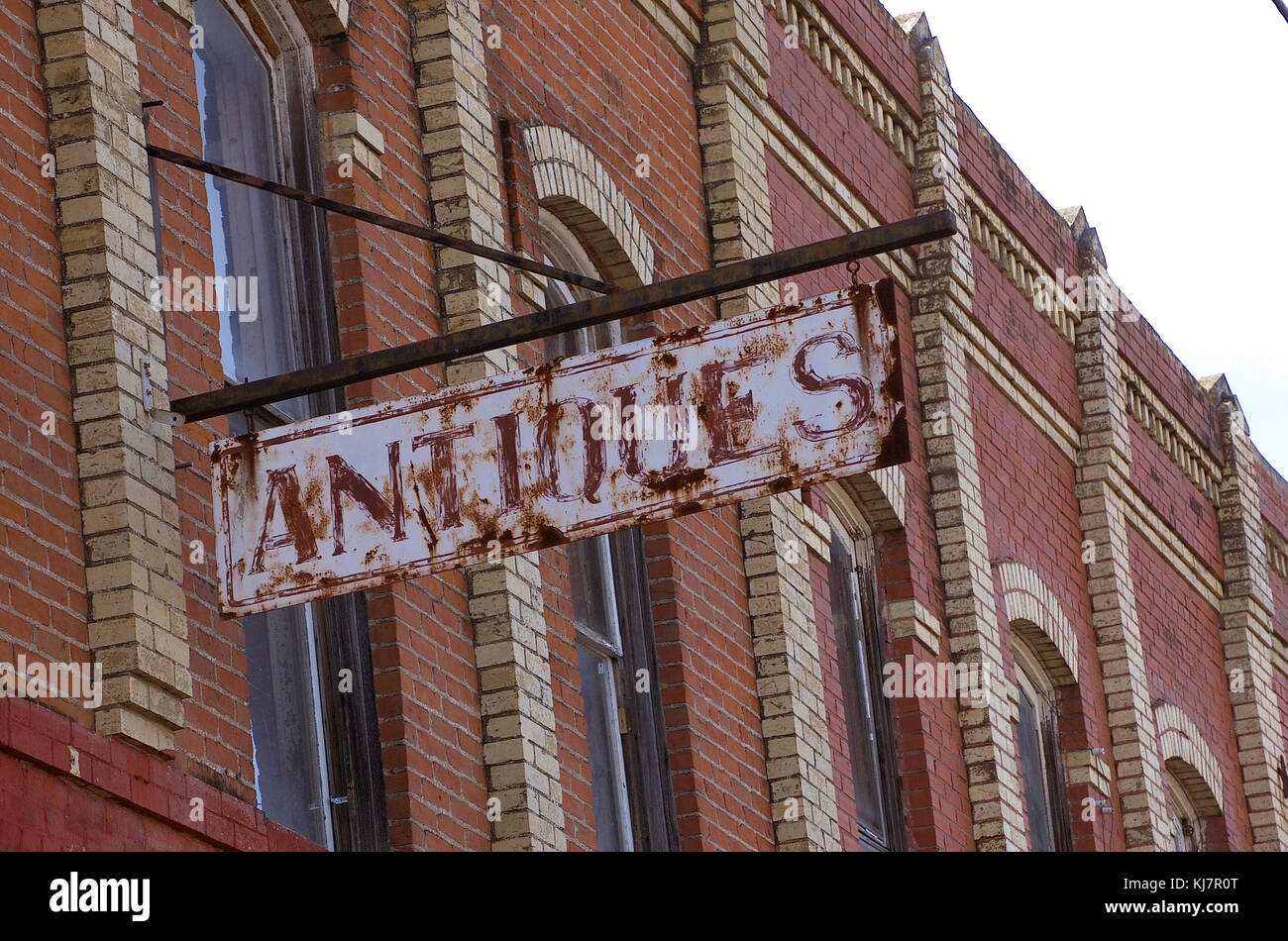 Worn antique sign hanging outside old brick building in business sector ...