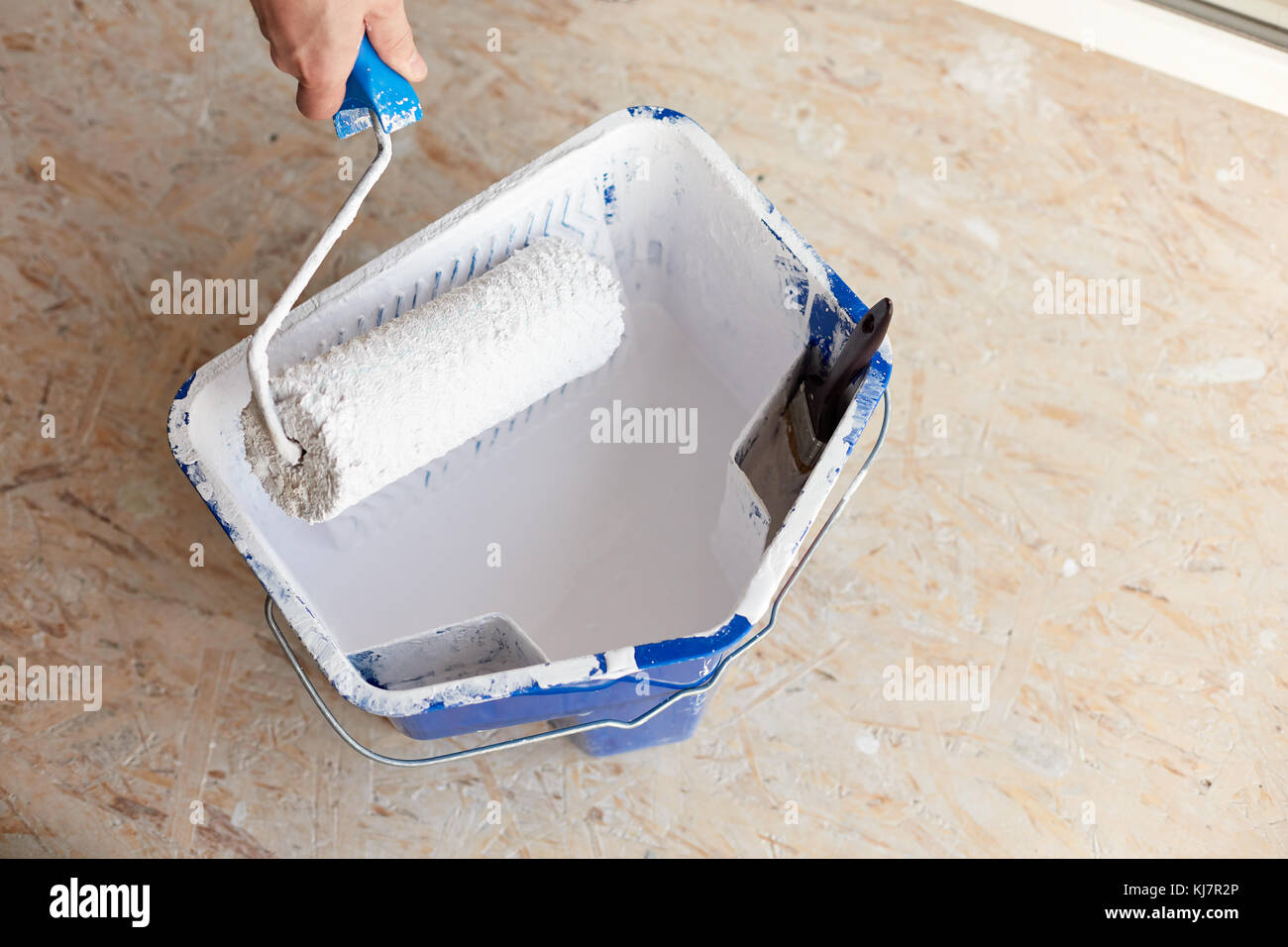 A bucket of white paint with a male hand holding a brush roller Stock ...