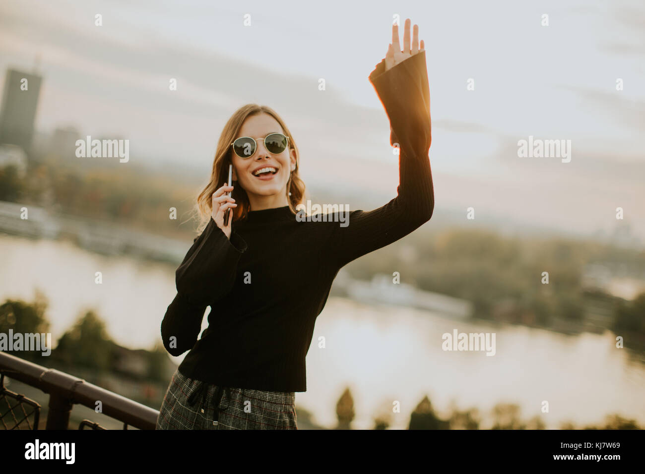 Portrait of young woman holding mobile phone while standing on walkway ...