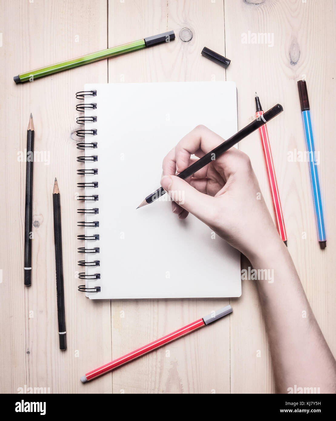 girl draws sketches in a notebook, lined near a variety of markers and ...