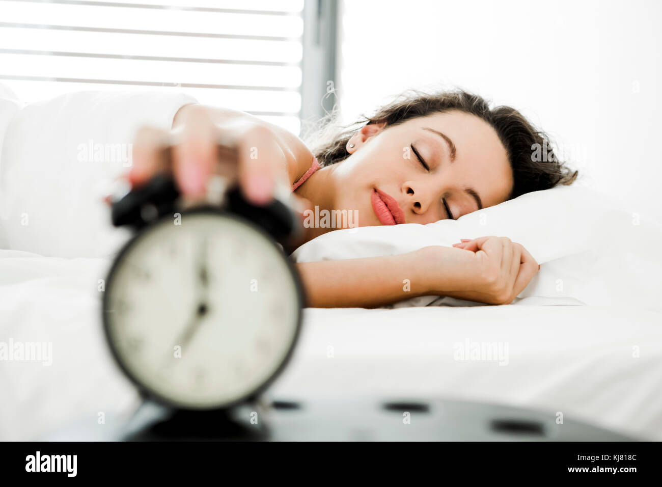 Beautiful young woman waking up with the alarm clock Stock Photo - Alamy