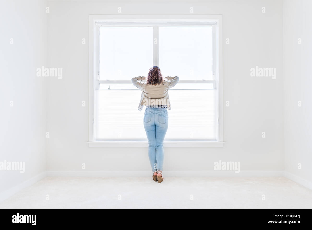 Back of one young woman standing in white, bright empty, clean room on ...