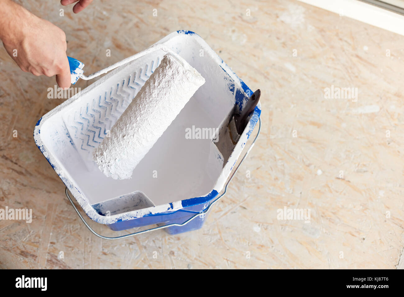 A bucket of white paint with a male hand holding a brush roller Stock ...