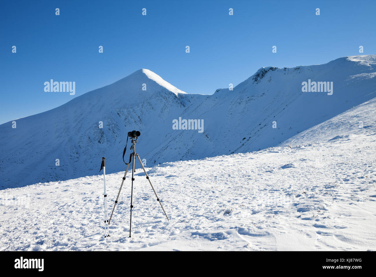 Tripod for photography with camera, ski poles on snow and snow-capped ...