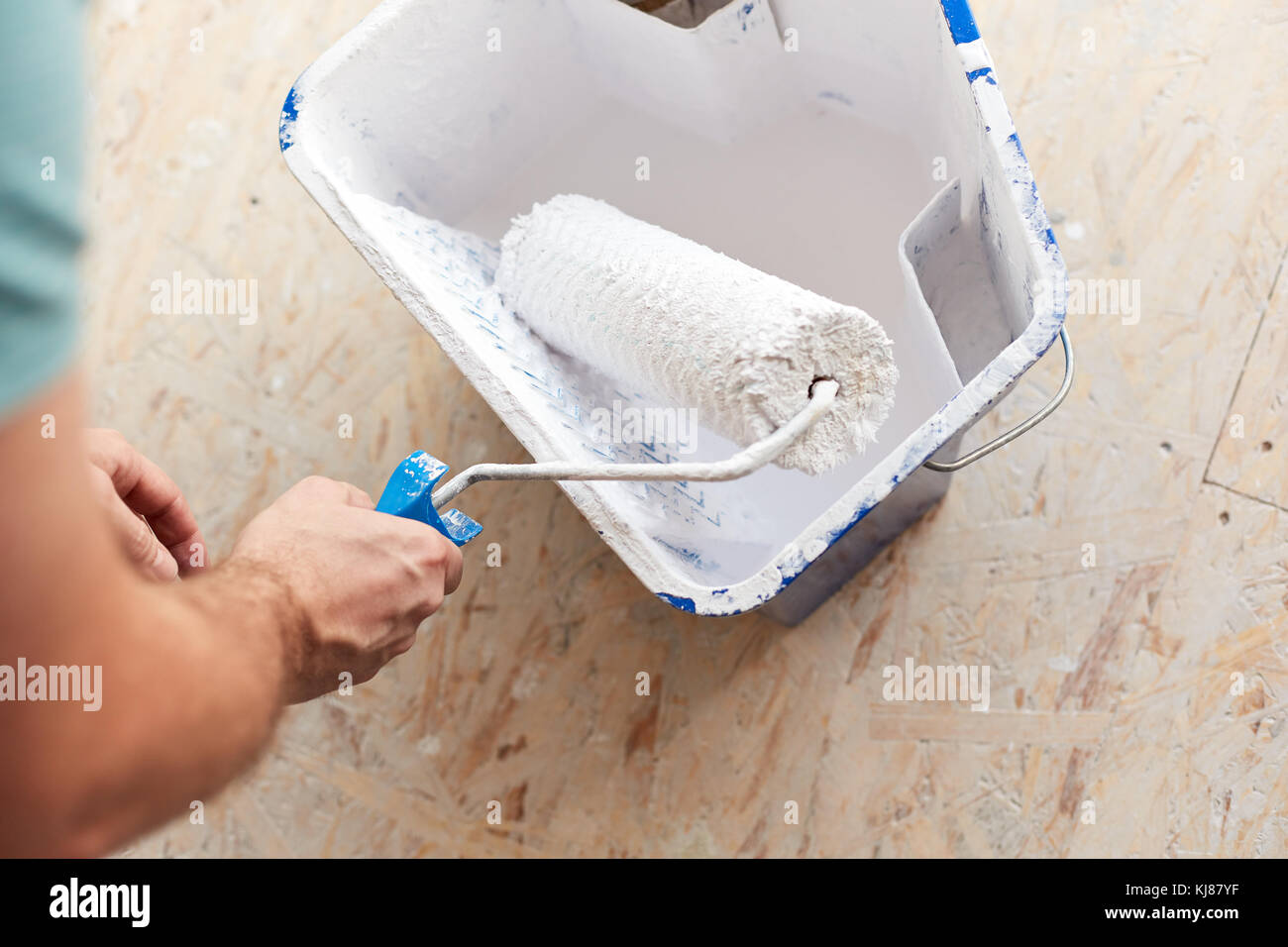 A bucket of white paint with a male hand holding a brush roller Stock ...