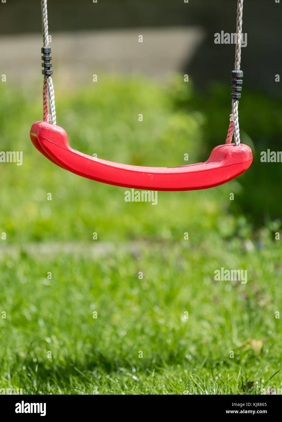 Detail of a red children's swing above green grass Stock Photo - Alamy