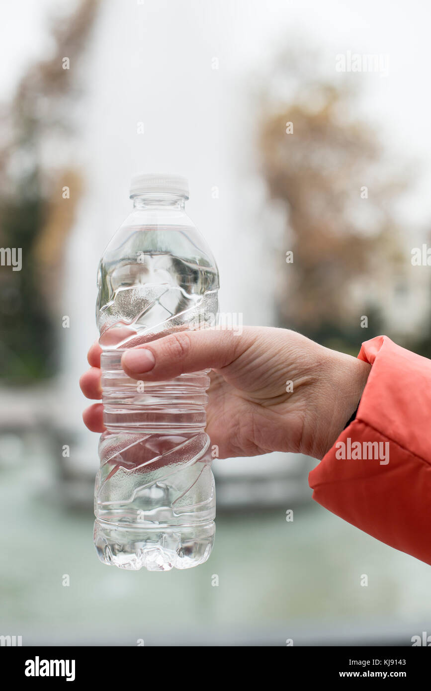 Bottle of water. Hand hold bottle mineral water in front of fountain ...