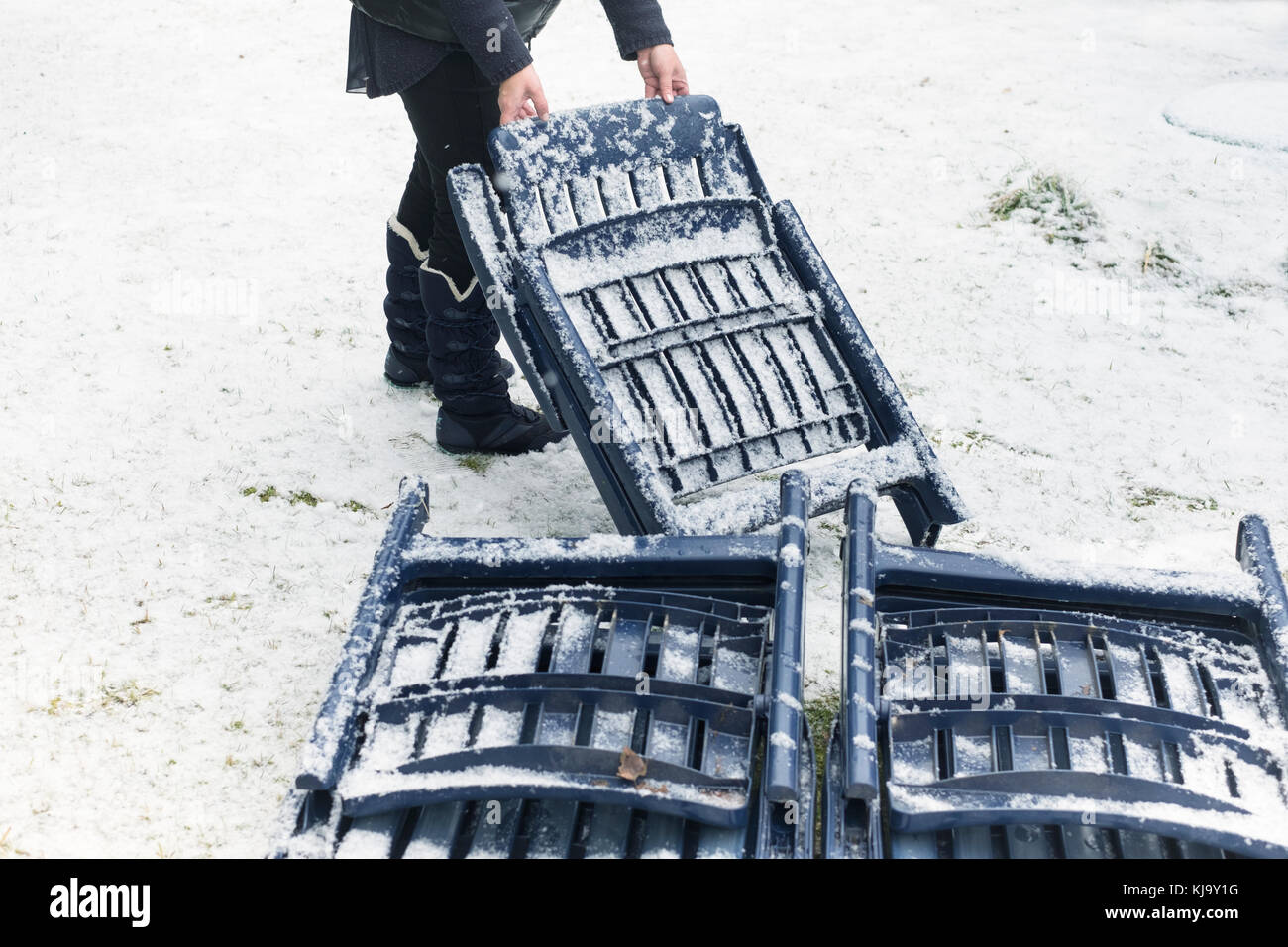 A woman moving plastic chairs under a snowfall in a backyard, outdoor ...