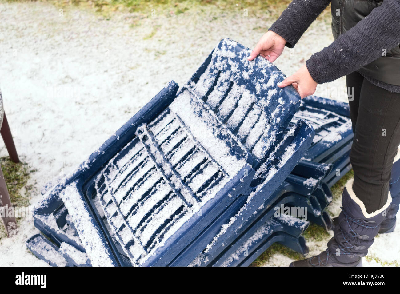 A woman moving plastic chairs under a starting snowfall in a backyard ...