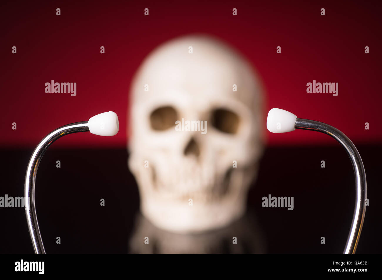 Stethoscope i focus and blurry skull isolated on black red background ...