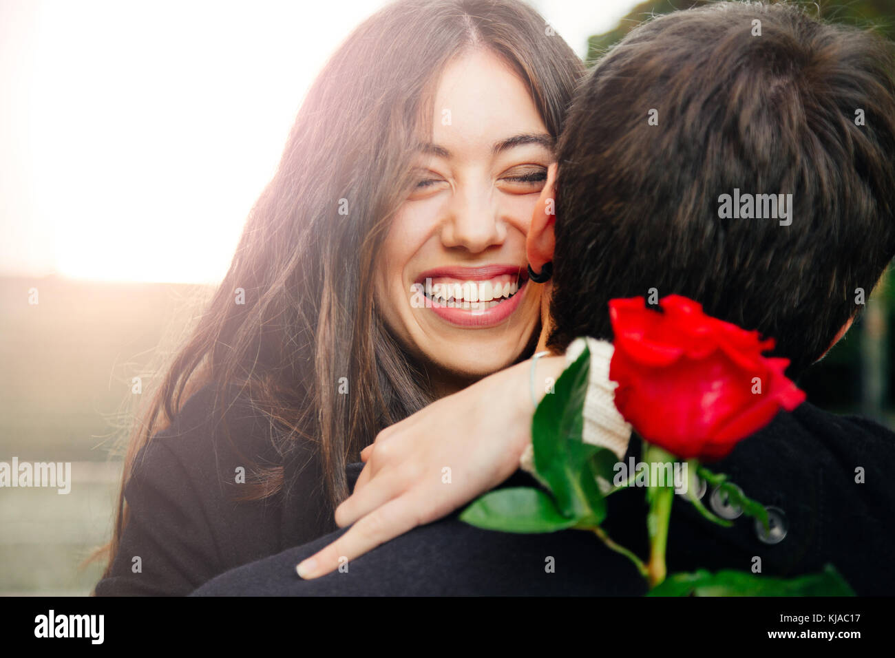 Beautiful and happy young woman in love hugging her boyfriend holding a red rose Stock Photo - Alamy