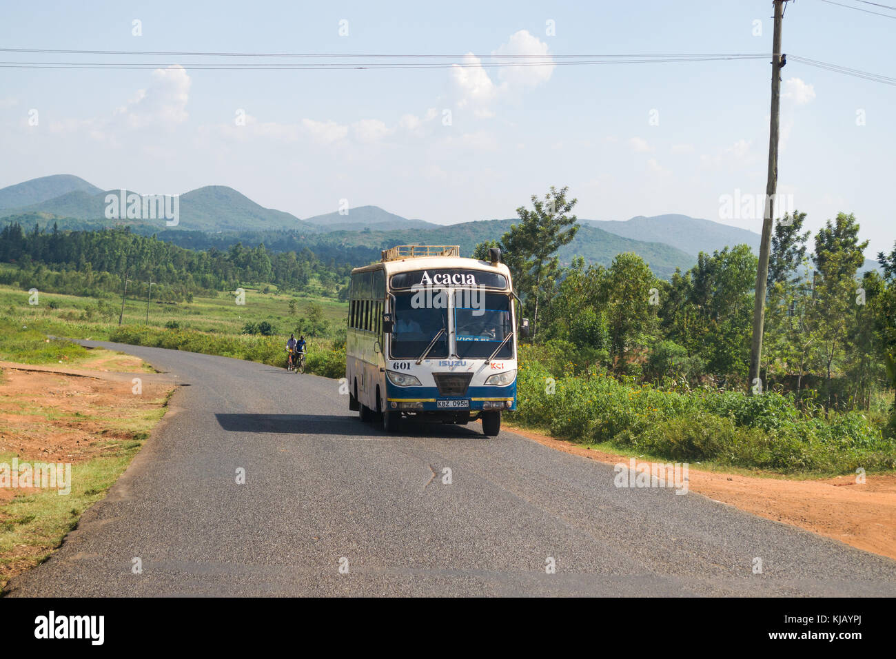 A bus drives along a countryside road with people on bicycles by the ...