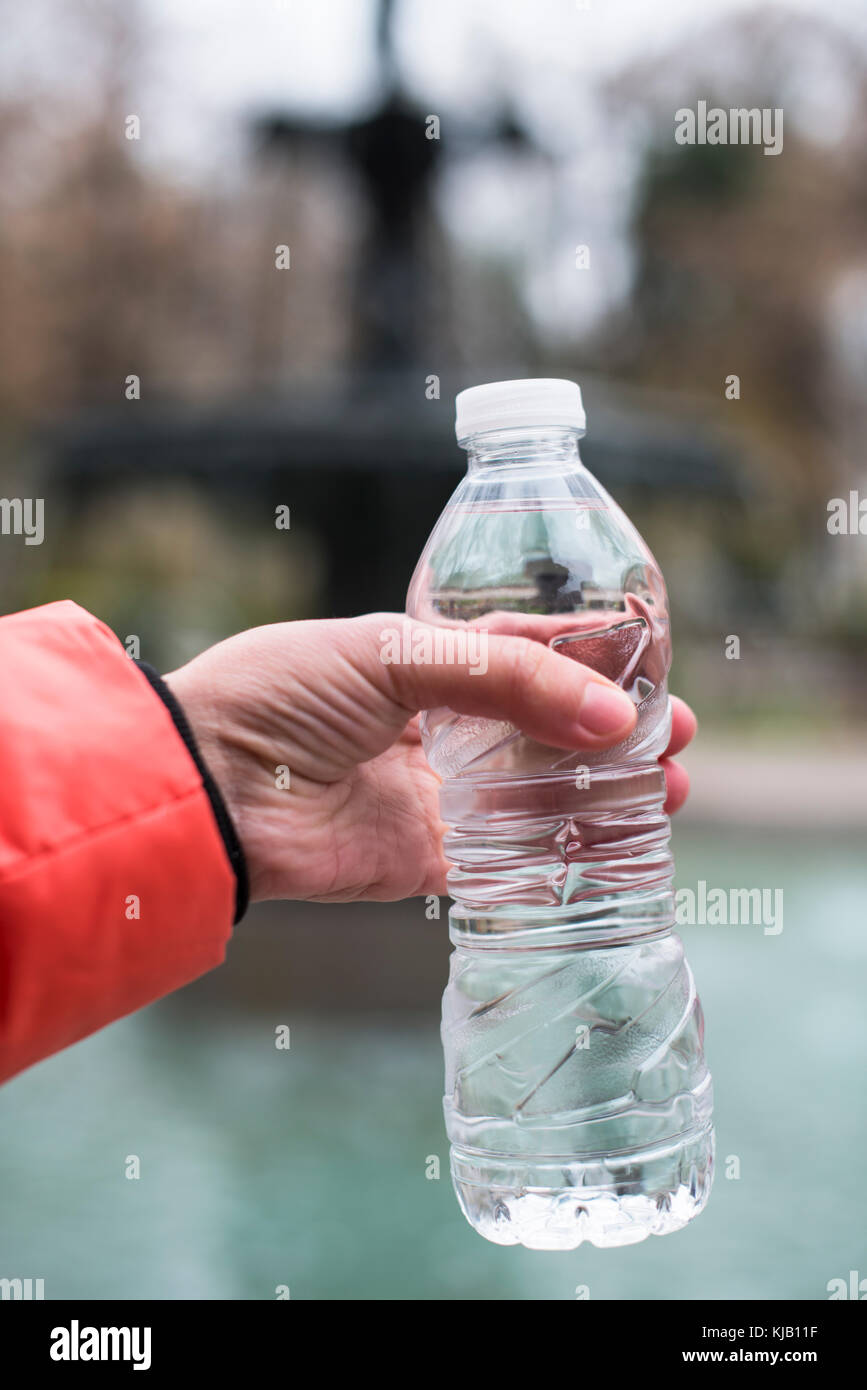 Bottle of water. Hand hold bottle mineral water in front of fountain ...
