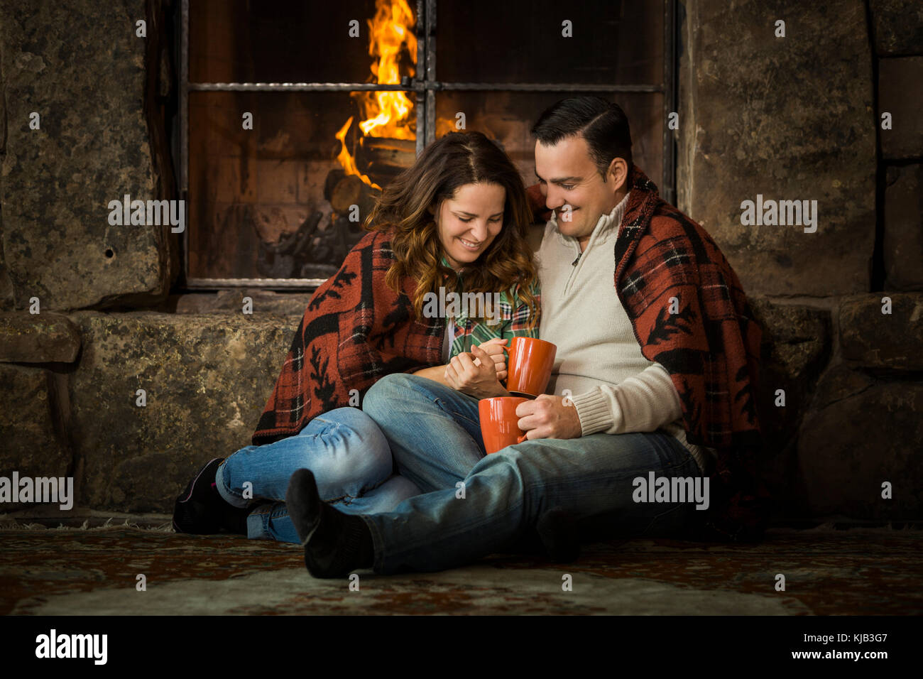 Smiling Caucasian couple cuddling on floor near fireplace Stock Photo ...