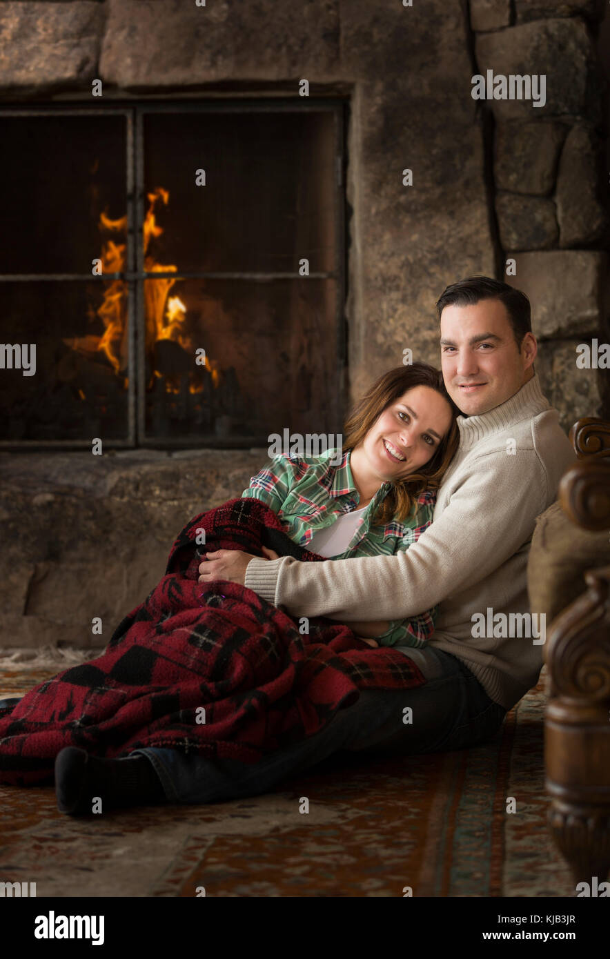 Smiling Caucasian couple cuddling on floor near fireplace Stock Photo ...