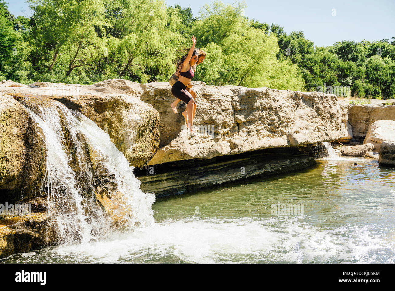 Caucasian couple jumping off rocks near waterfalls Stock Photo - Alamy