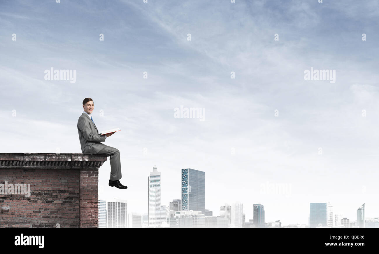 Man on roof edge reading book and cityscape at background Stock Photo ...