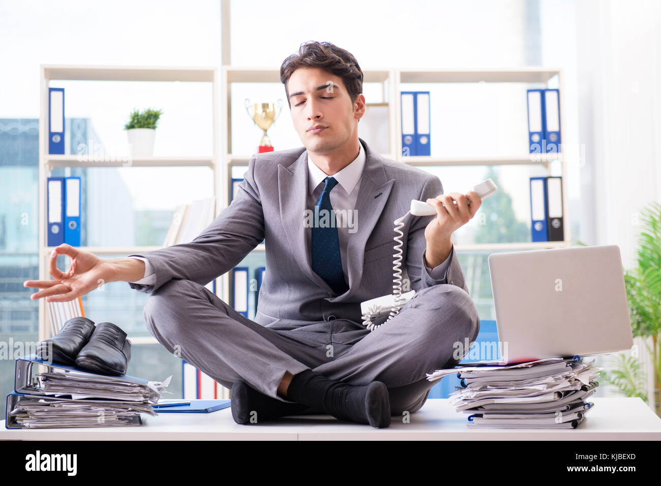 Businessman sitting on top of desk in office Stock Photo - Alamy