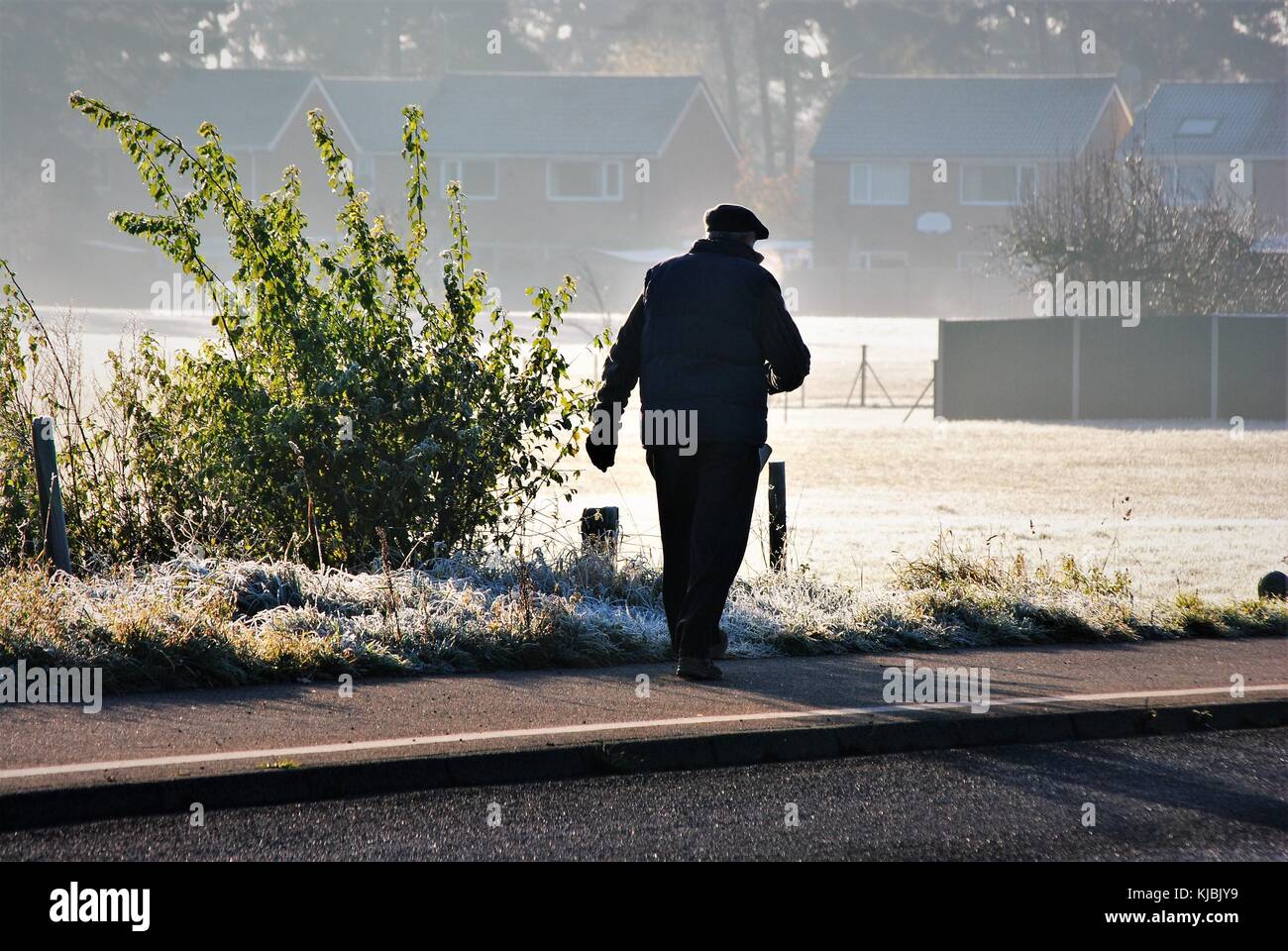 Man walking on path beside field towards town on bright and frosty ...