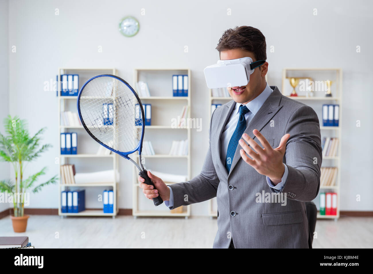 Businessman playing virtual reality tennis in office with VR goggle ...