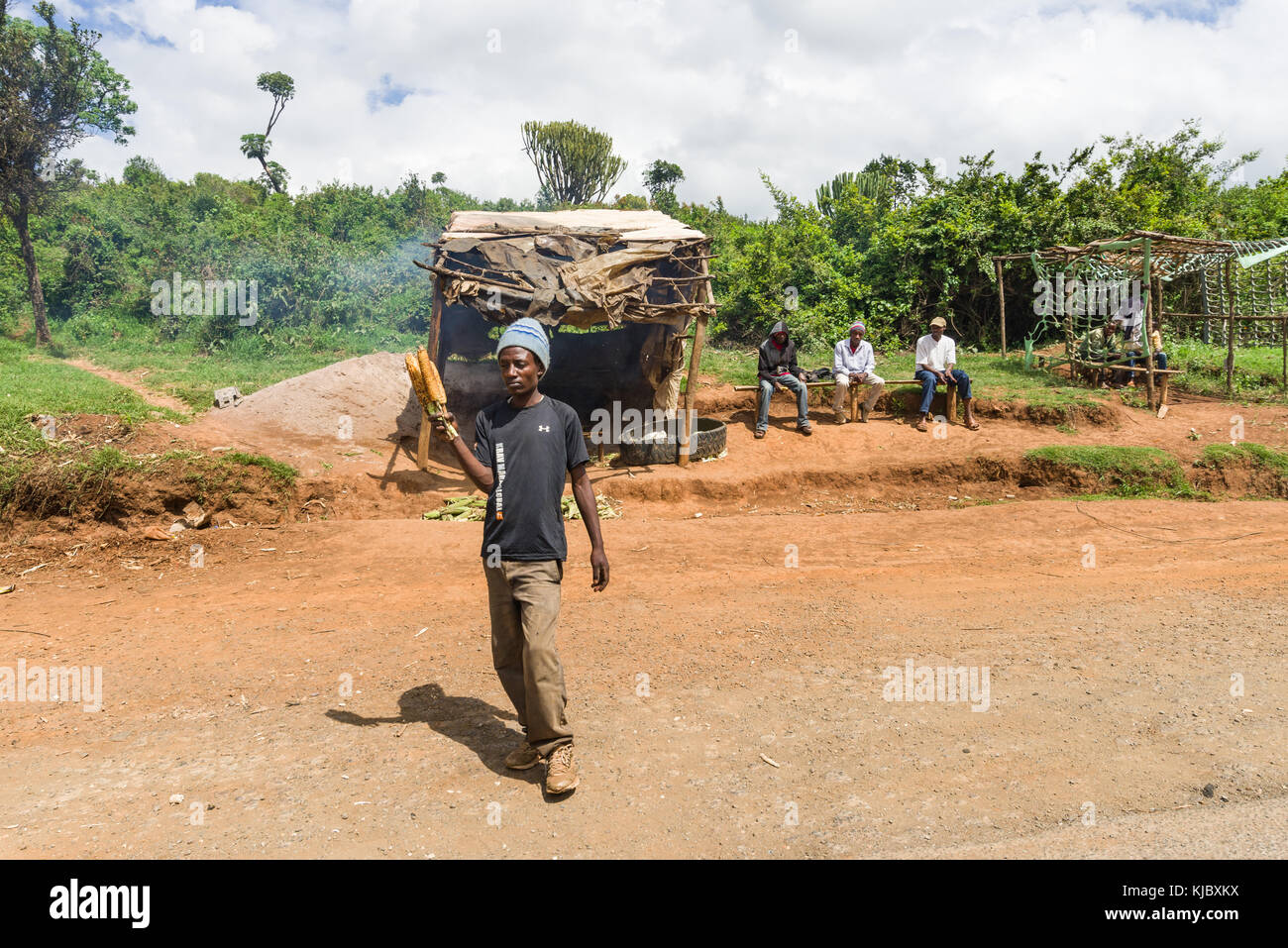 A man stands by the roadside holding cooked maize for sale whilst other ...