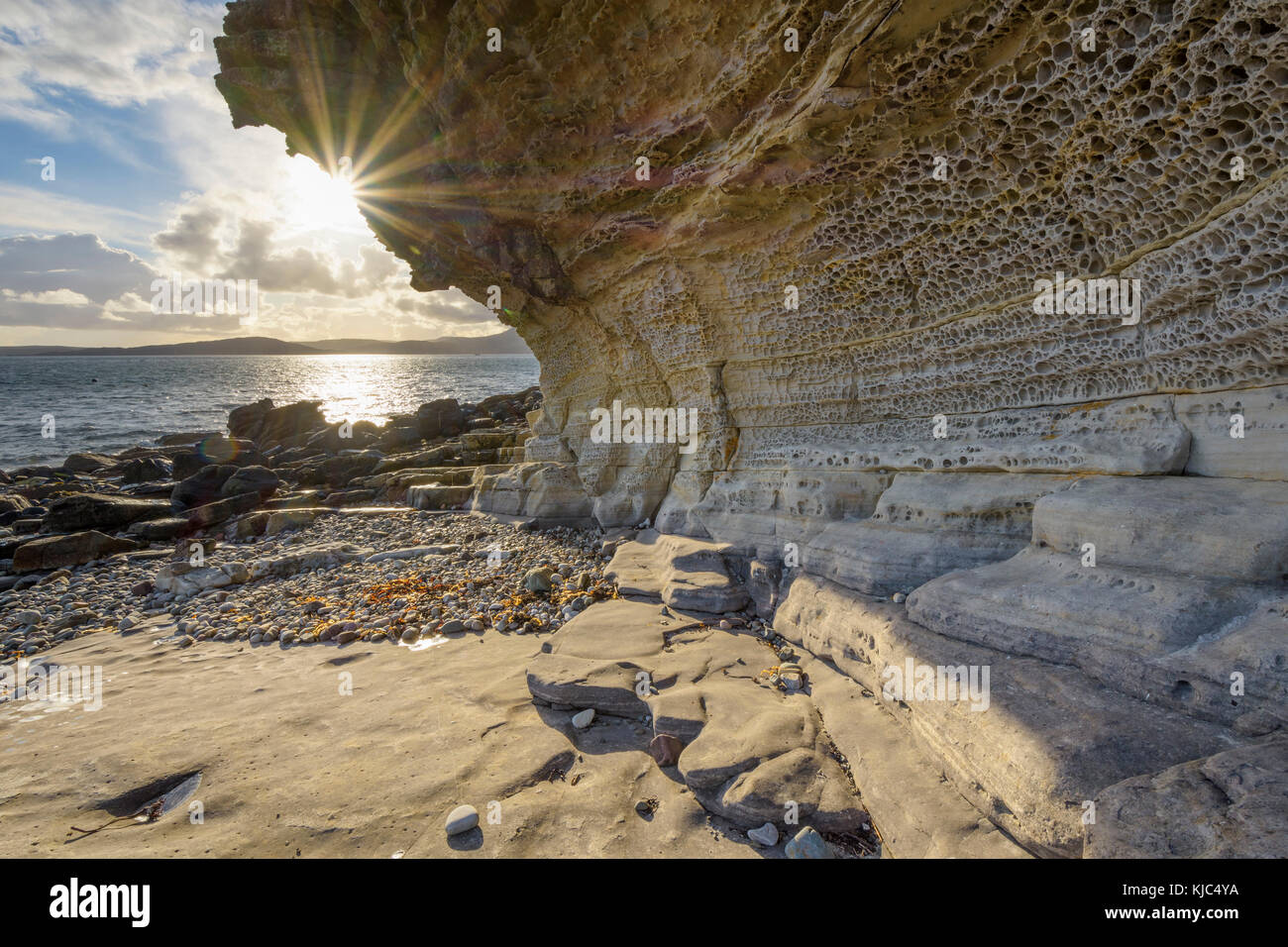 Close-up of rock face of sea cliff with honeycomb weathering and sun ...
