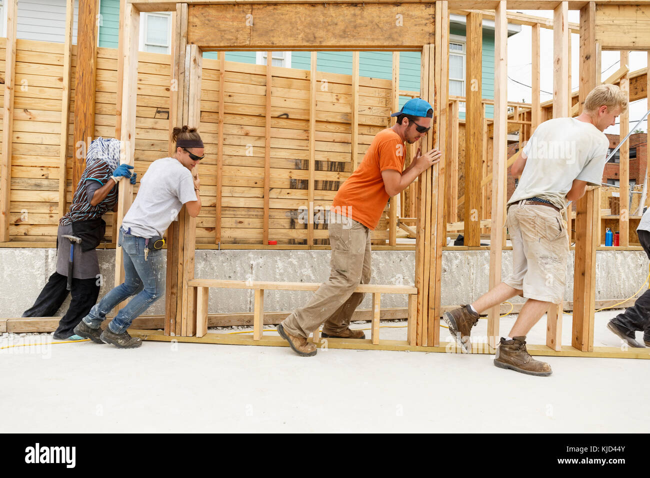 Volunteers pushing framed wall at construction site Stock Photo - Alamy