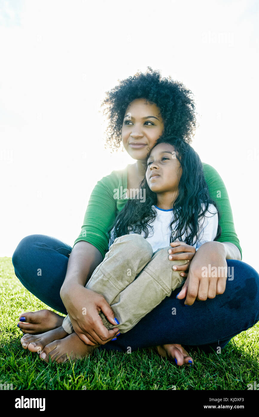 Portrait Of Pensive Mixed Race Mother And Daughter Sitting In Grass