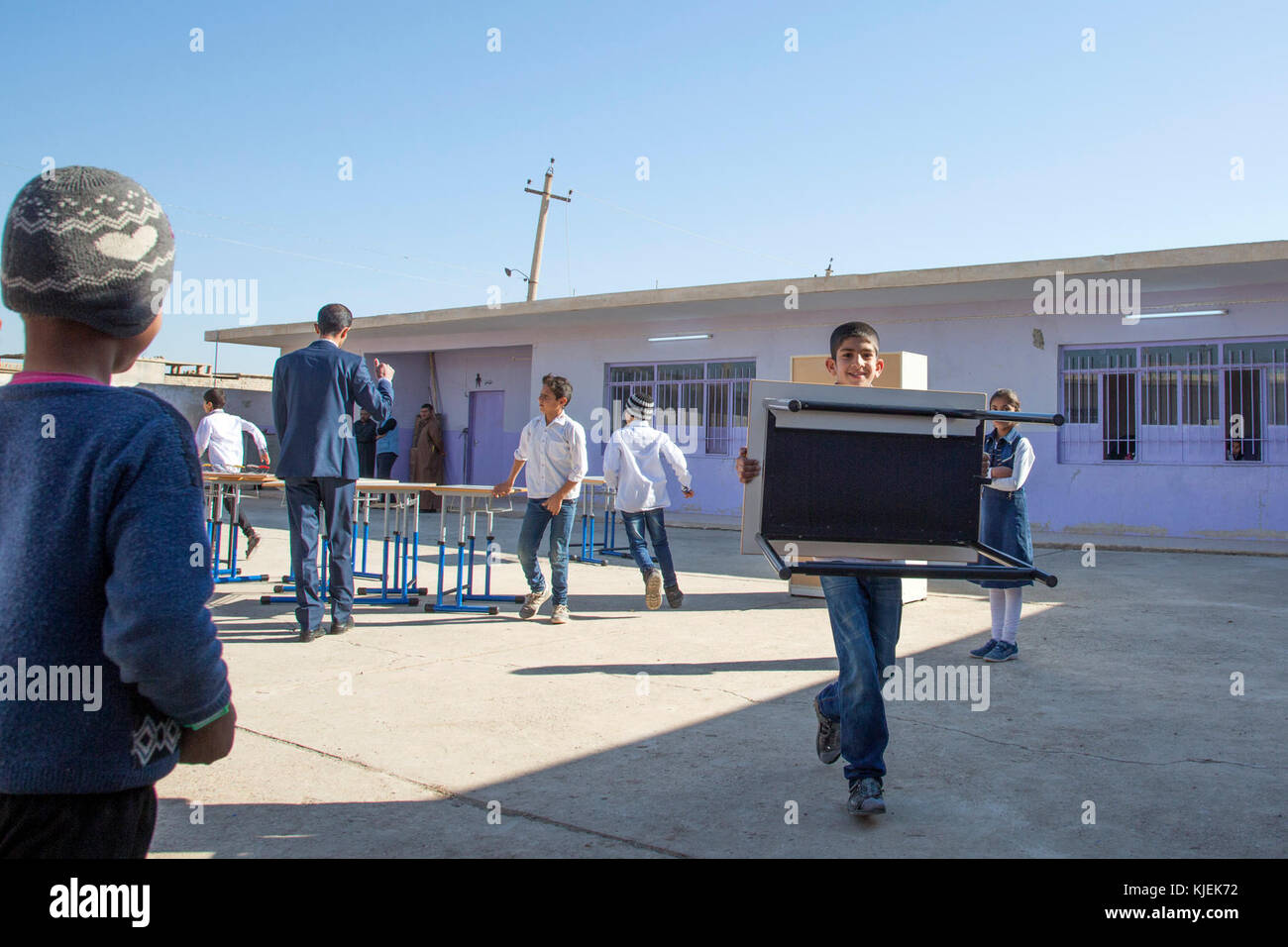 An Iraqi student carries a desk donated by the Italian army into a ...