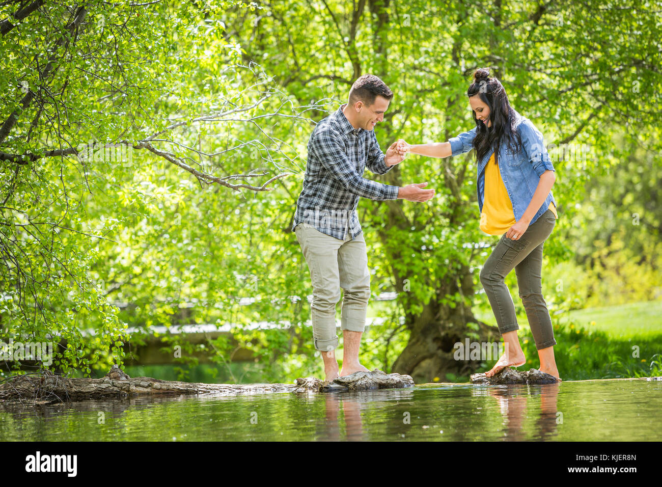 Man helping woman standing on rocks crossing river Stock Photo - Alamy