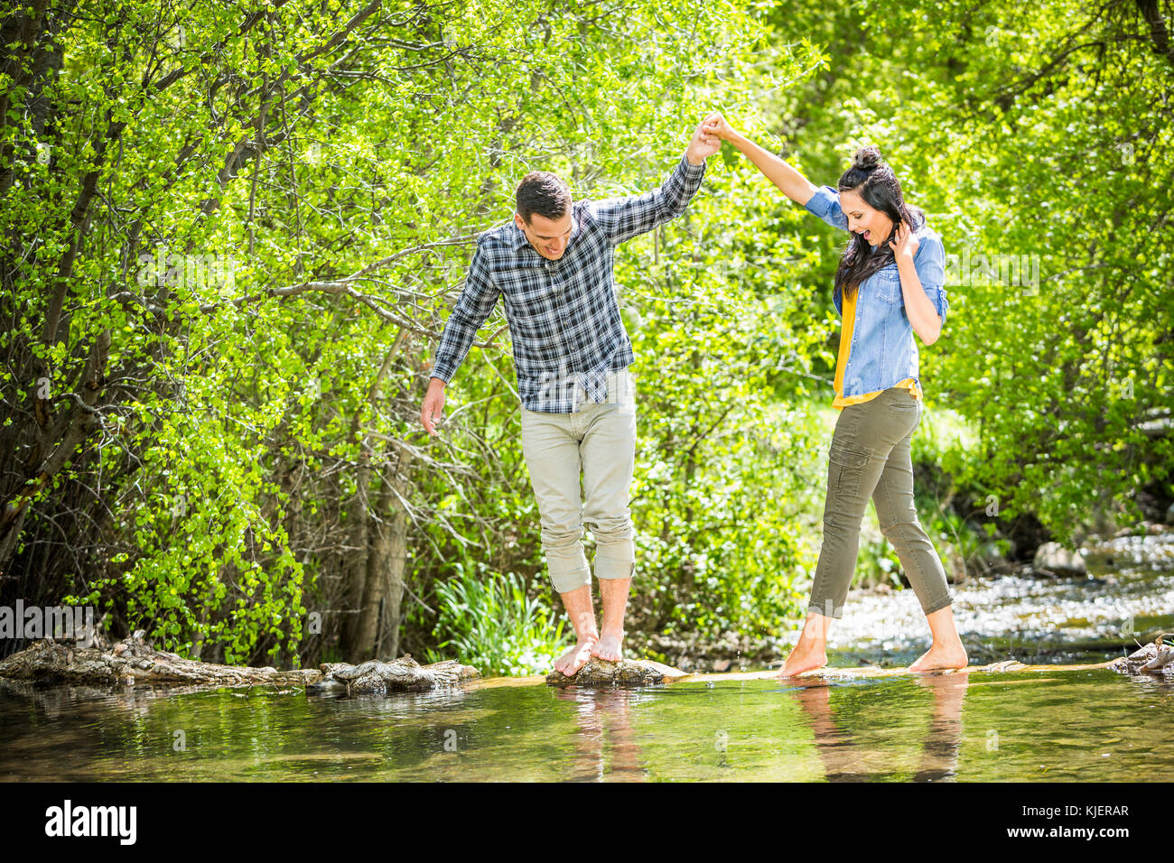 Man helping woman standing on rocks crossing river Stock Photo - Alamy